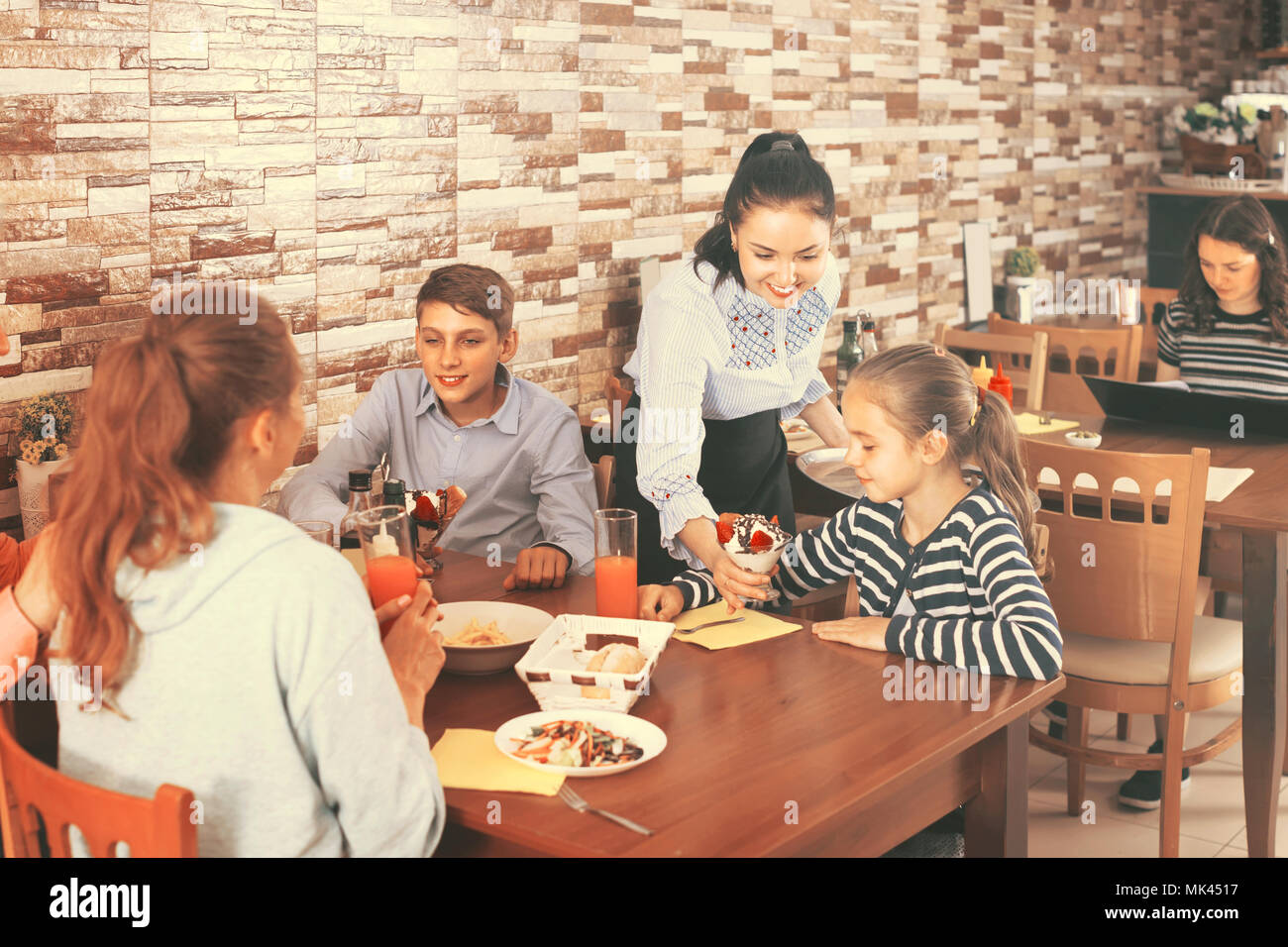 courteous brunette waitress serving cheerful family in comfy family ...