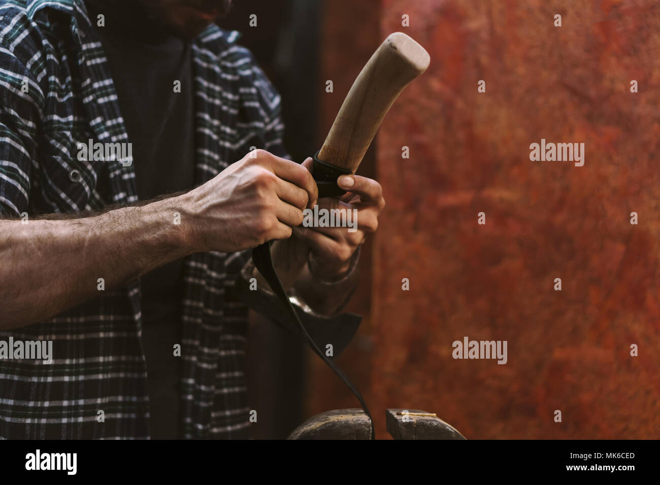 Man working in carpentry workshop. He wraps wooden handle of ax with ...