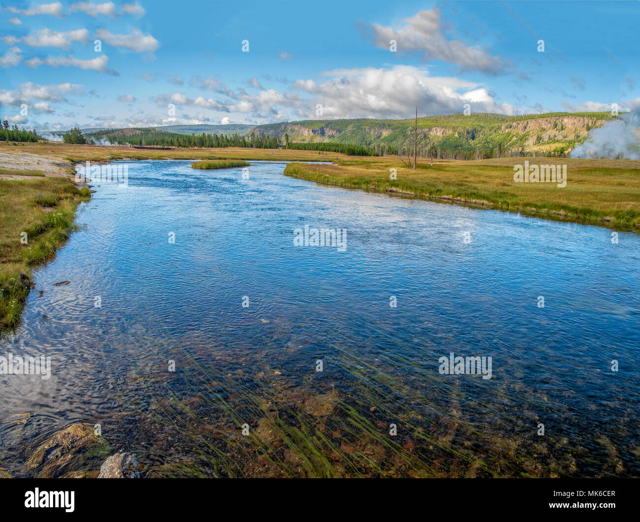 Slow moving river with green meadows heading toward mountains in the ...
