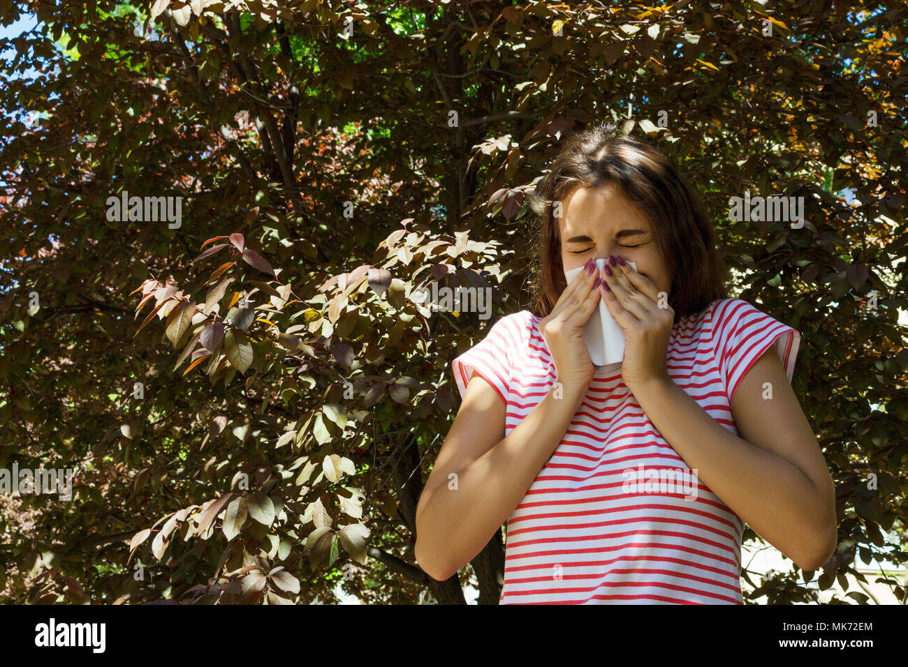 Young girl with allergy in autumn park. Sneezing girl blows her nose in ...