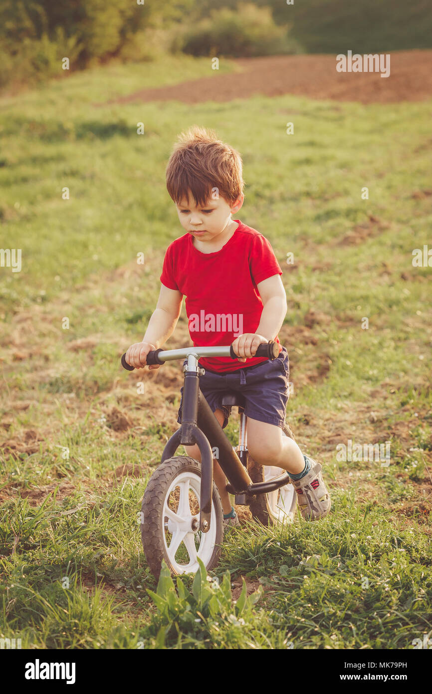 Little boy rides a balance bike in the countryside at sunset. Run ...