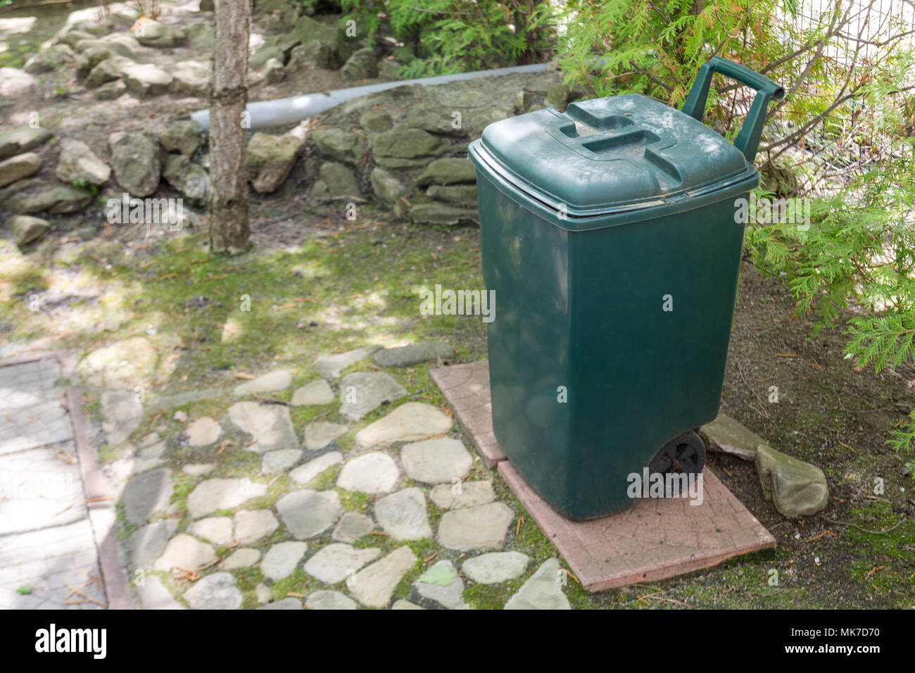 Green plastic garbge bin in garden.Single garbage container stand in ...