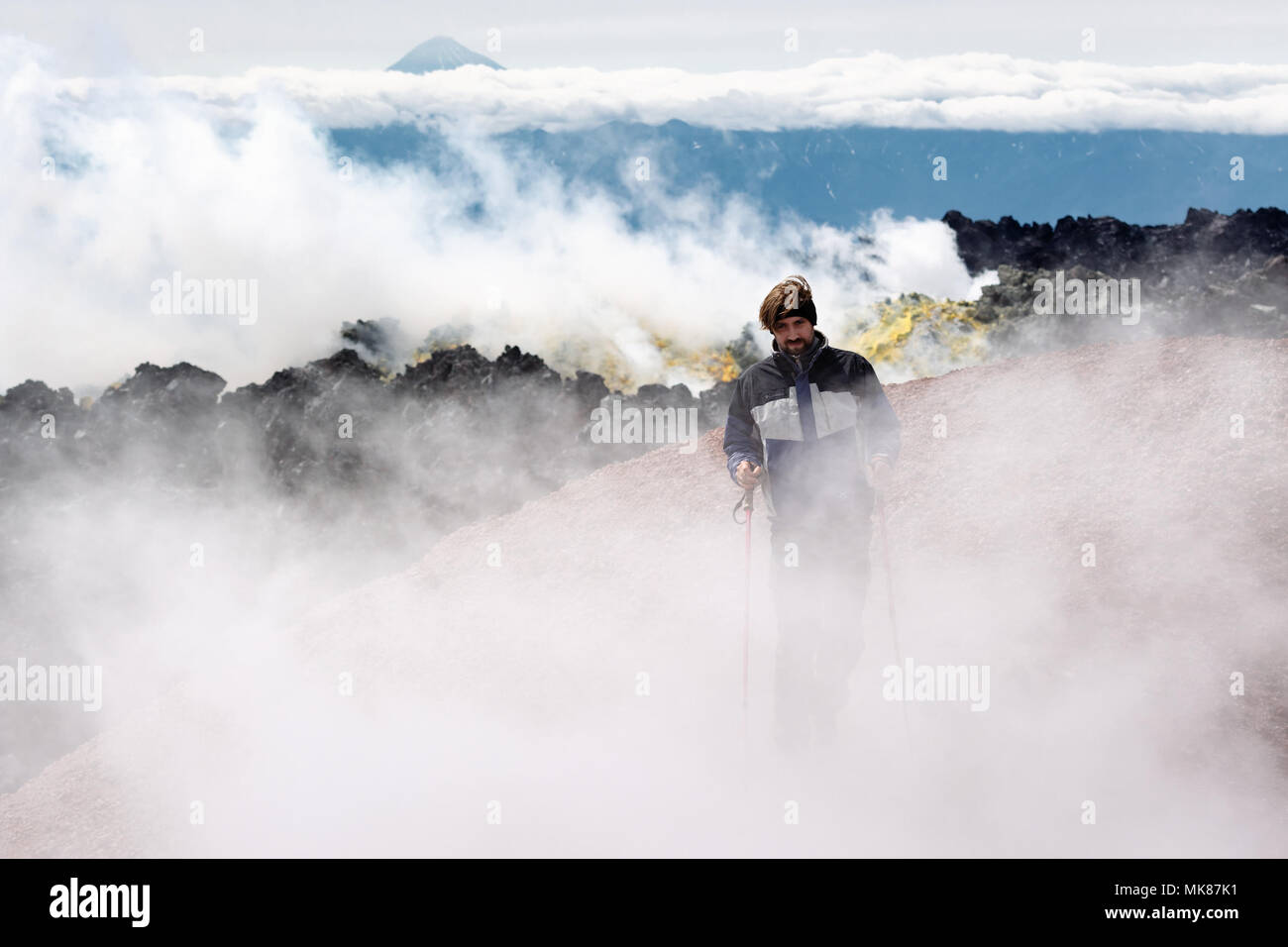 Hiker climbing on lava field in clouds of volcanic steam and gas in ...