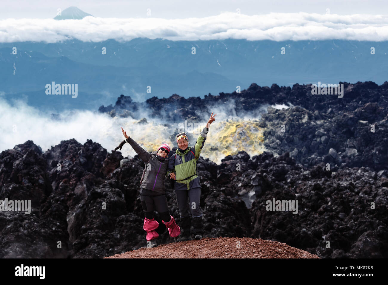 Girlfriends stand in crater of active volcano on background of piles of ...