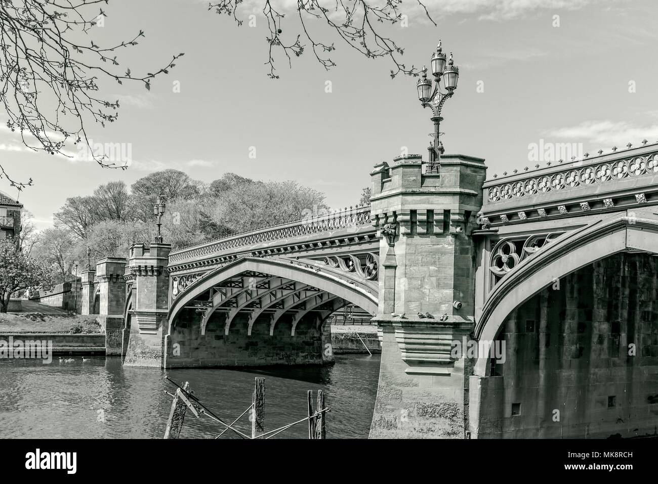 Bridge constucted of stone and iron spans the River Ouse in York. Trees ...