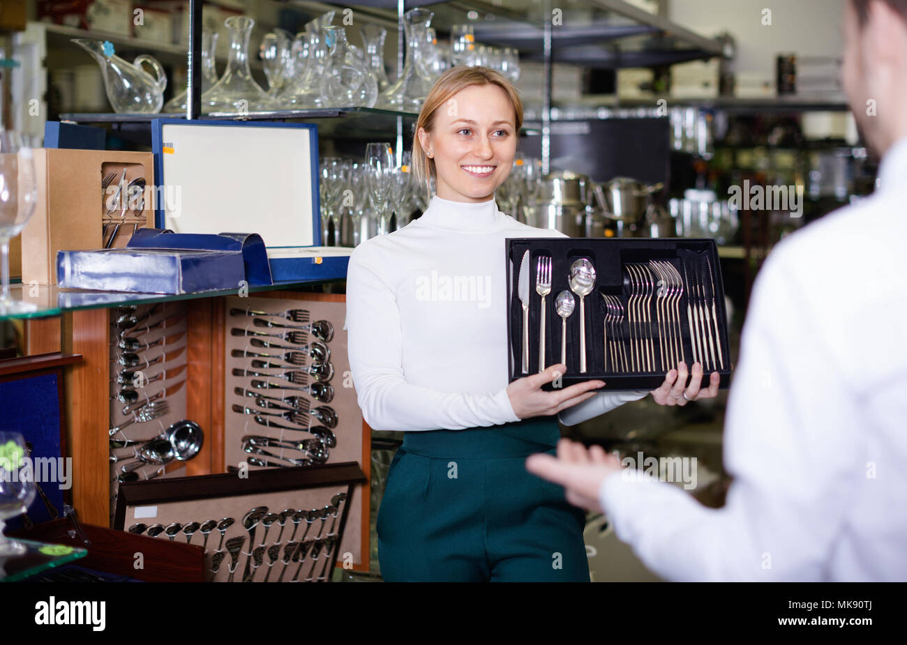 Happy cheerful female shopping assistant offering cutlery in dinnerware ...