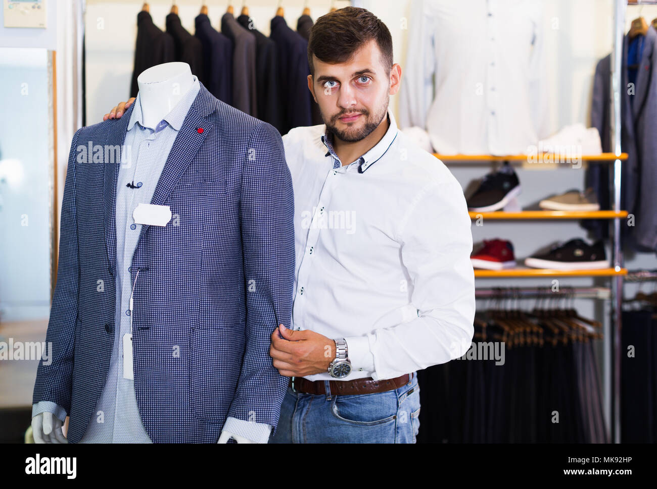 positive young owner guy displaying jacket in fashion store Stock Photo ...