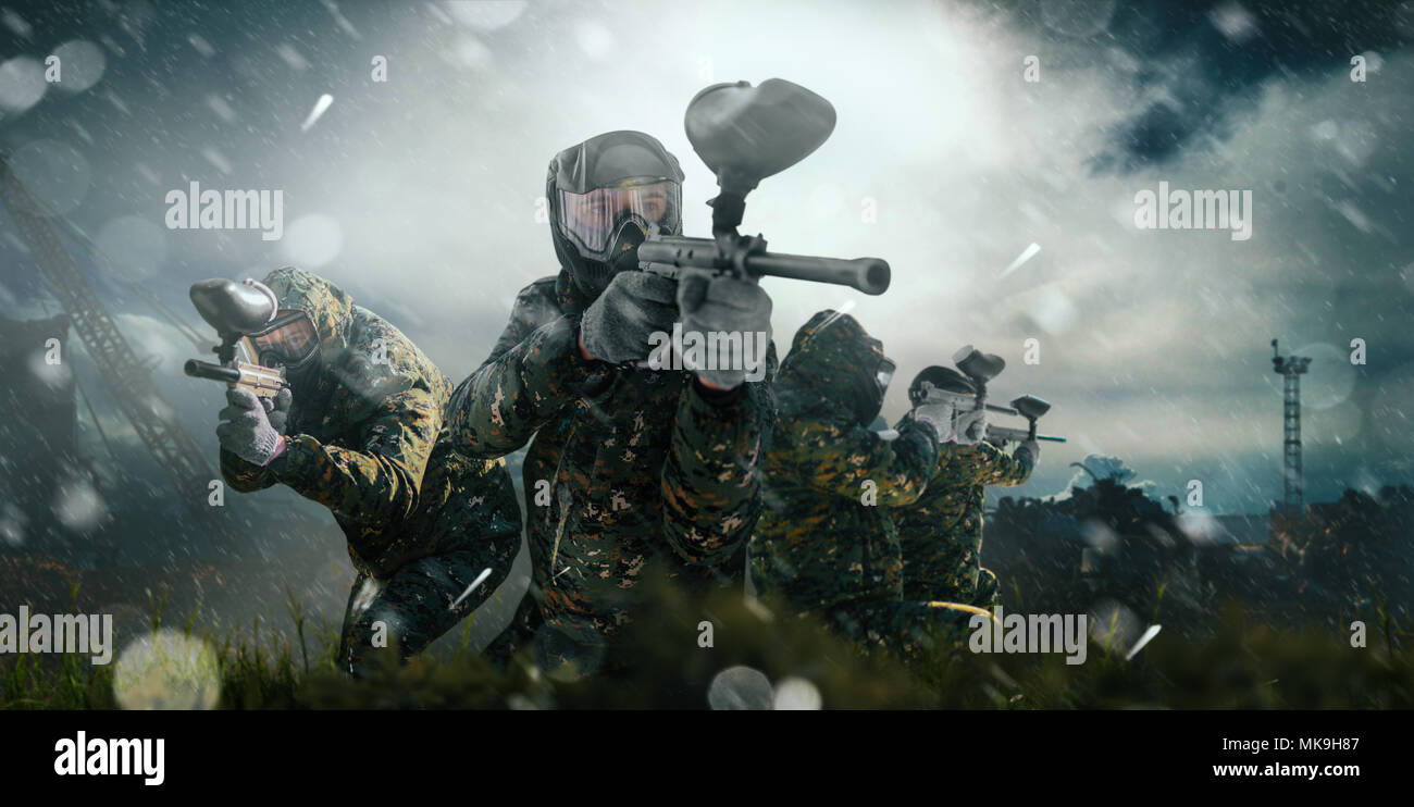 Paintball team in uniform and masks stood around with markers in hands ...