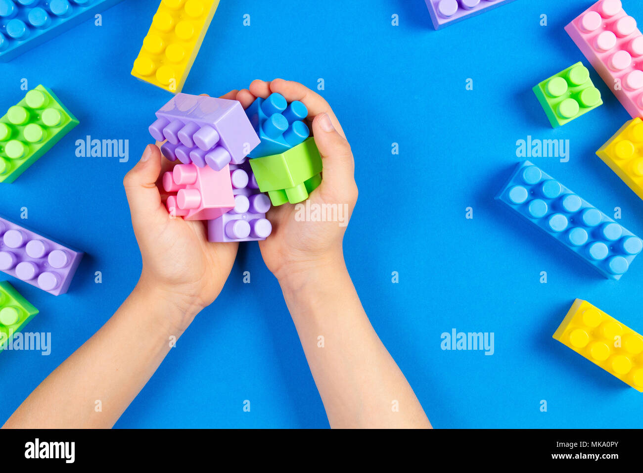 Kids hand playing with colorful plastic construction blocks on blue ...