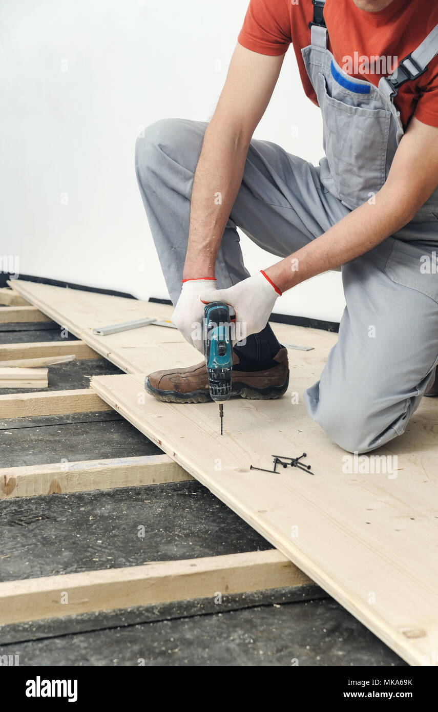 Installation of wooden floors. Worker twisting screw into the floor ...