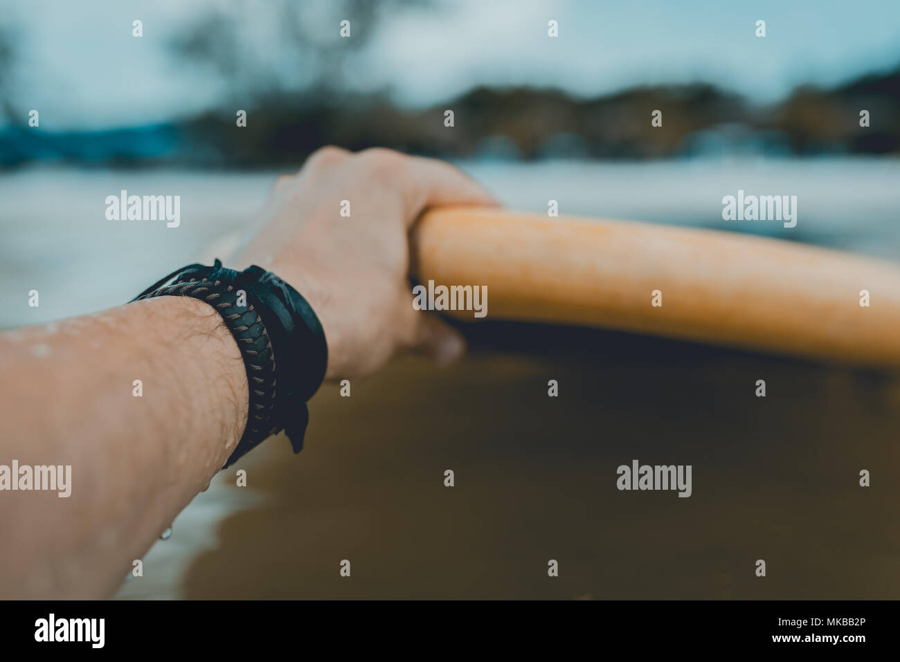 Man’s hand holding paddleboard front. Leather strip on the forearm ...