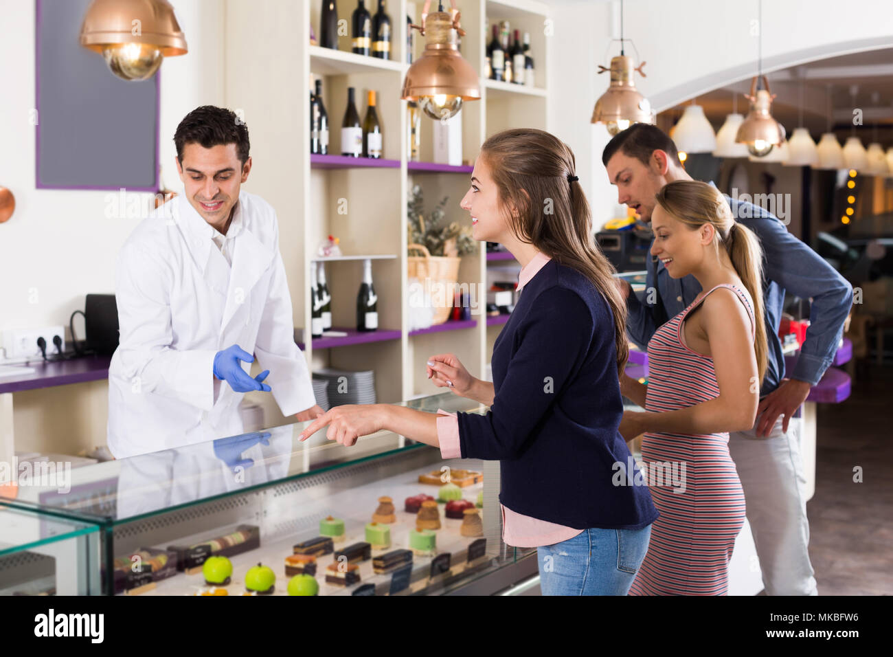 Hospitable man confectioner serving visitors in cozy pastry store Stock ...