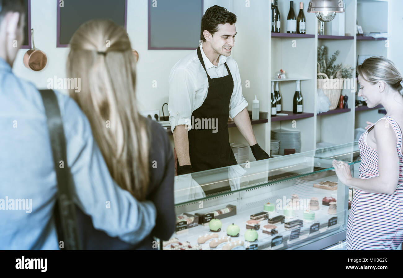 Smiling man confectioner serving visitors in confectionery cafe Stock ...