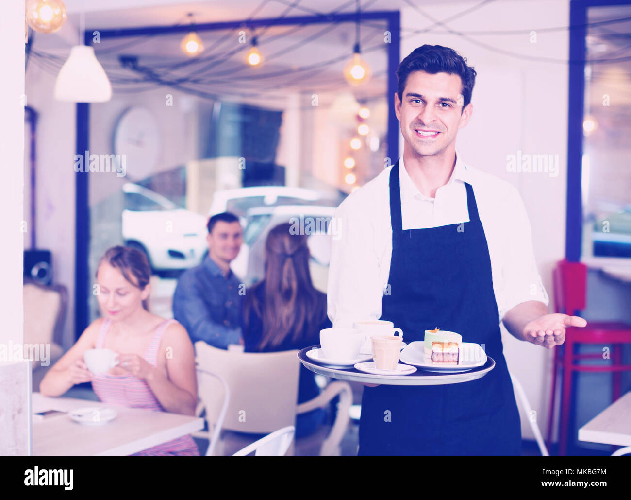 Cheerful positive smiling waiter holding served tray meeting visitors ...