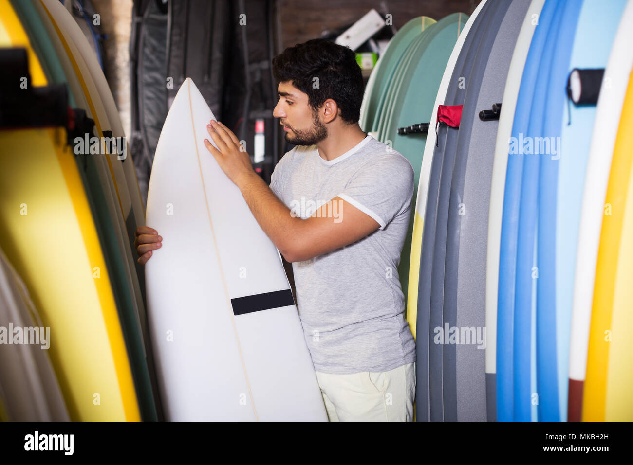 positive male surfer holding professional surfboard in the shop for ...