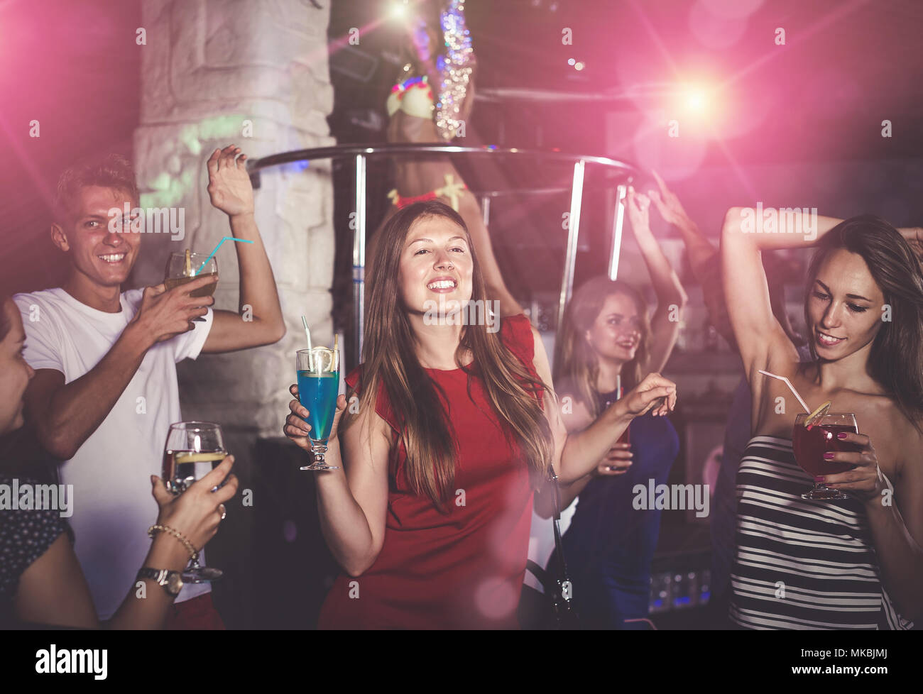 Positive men and women joying and dancing with drinks on party in the ...