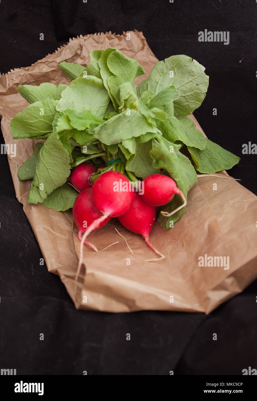 Raw radishes with leaves on paper bag and black background Stock Photo ...