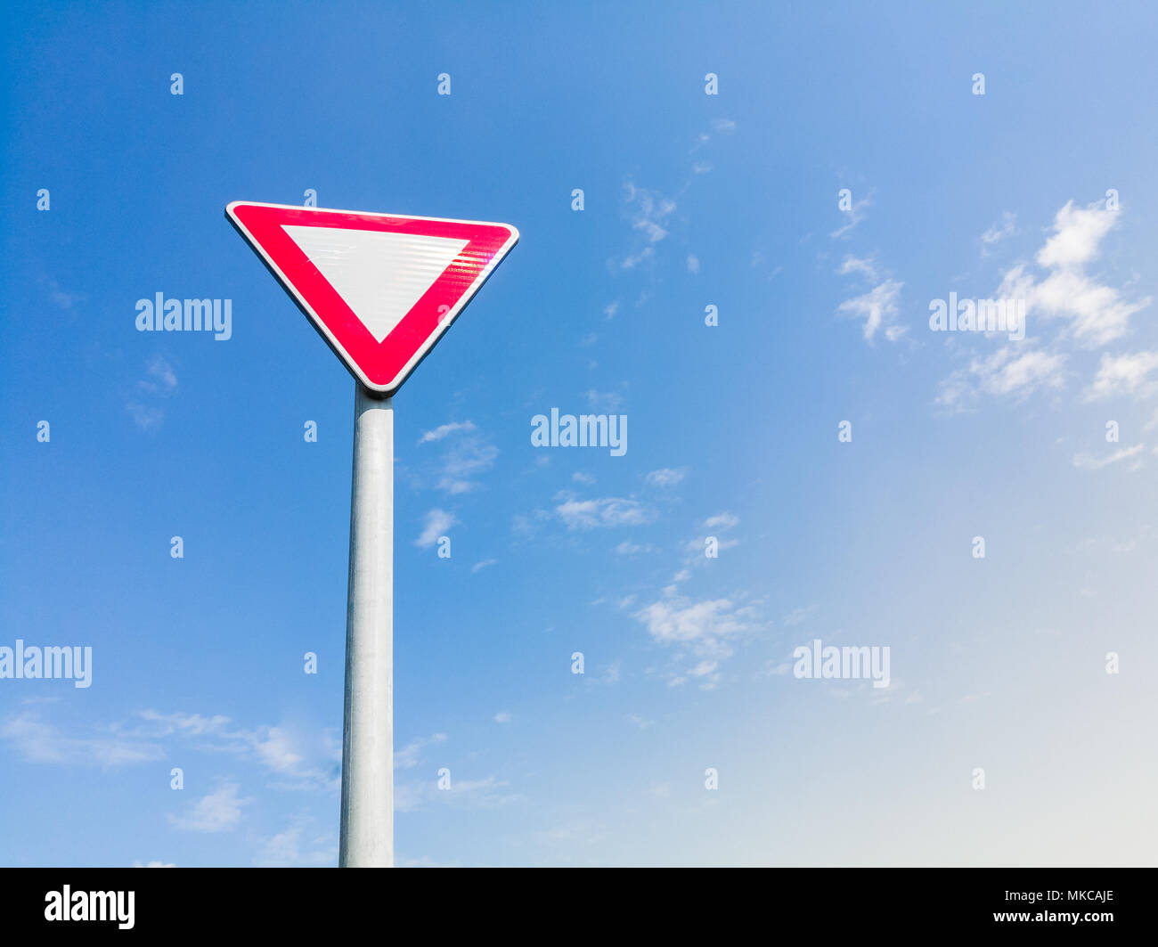 A road give way signal with a blue sky and clouds in the background ...