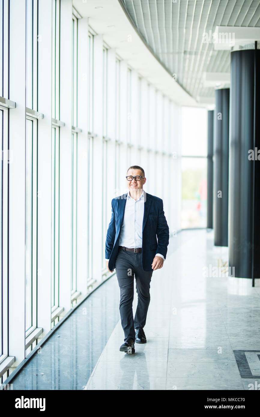 Mid aged business man walking towards the camera and smiling in office ...