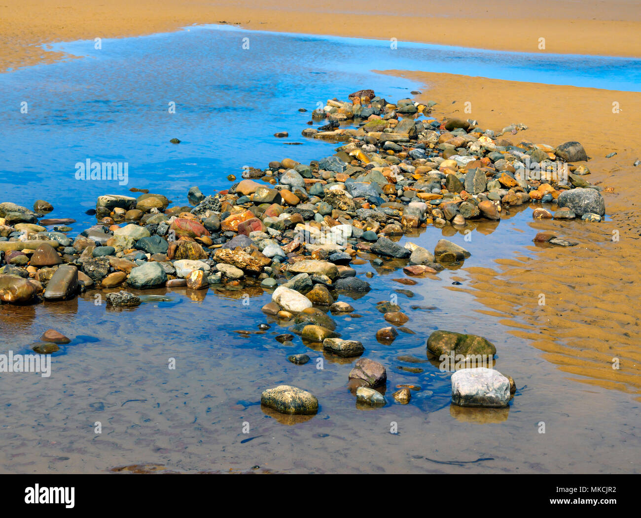 Pool on a sandy beach at low tide with cobbles and small sea worn rocks ...