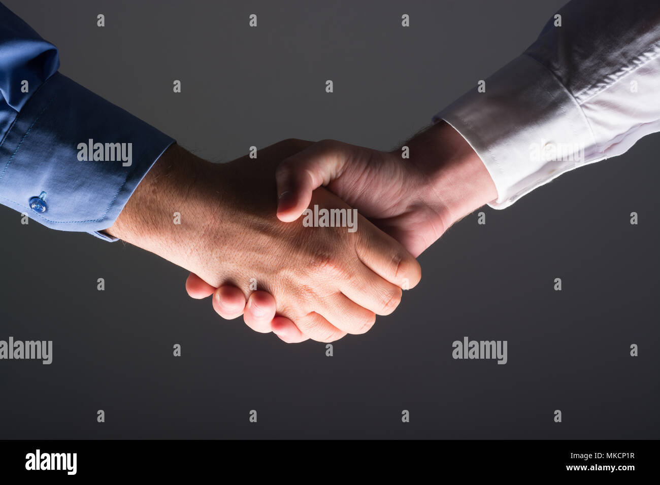 Low angle view of two businessmen hands shaking over dark gray ...