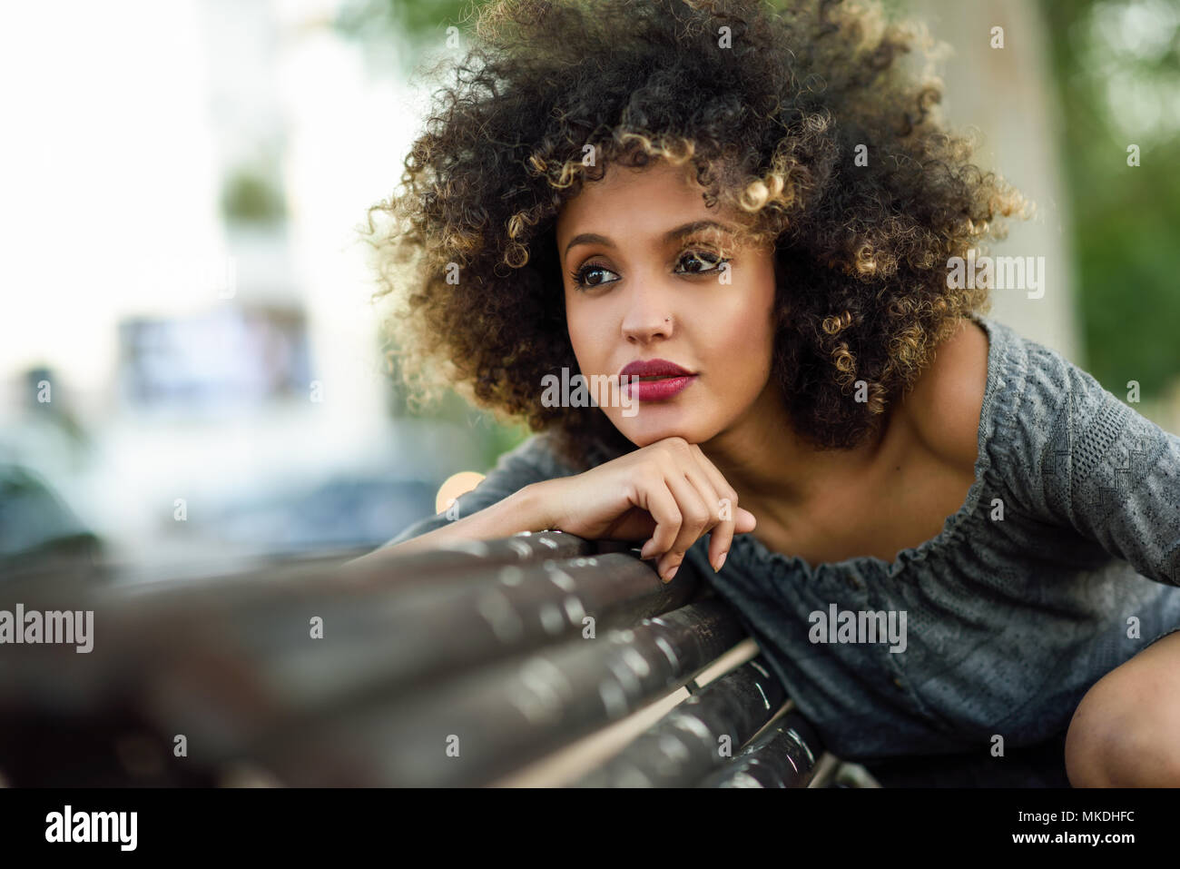 Young black woman with afro hairstyle sitting on a bench in urban ...
