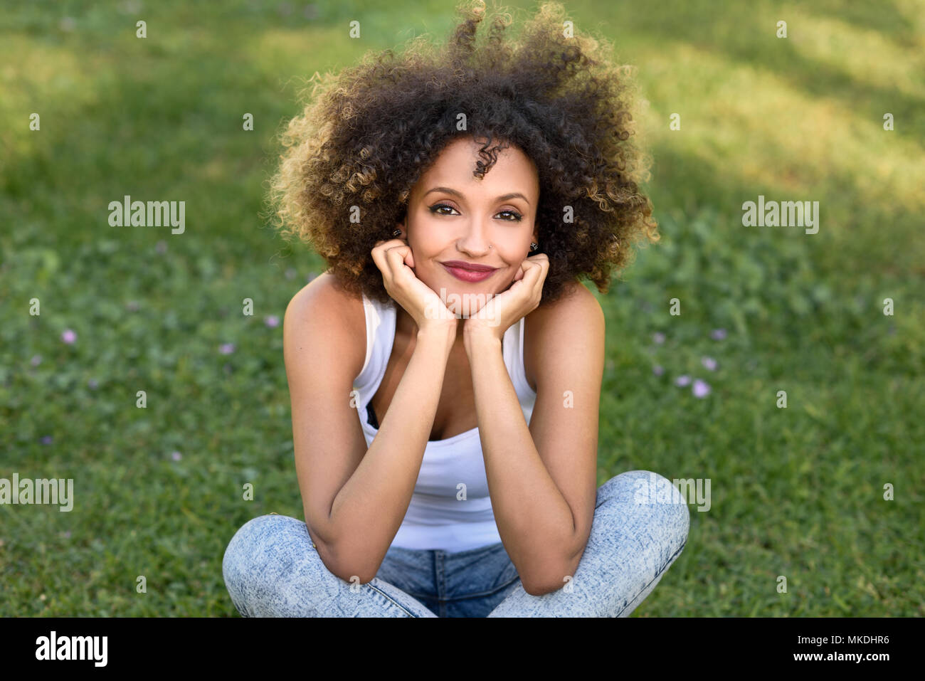 Mixed woman with afro hairstyle smiling in urban park. Young black girl ...