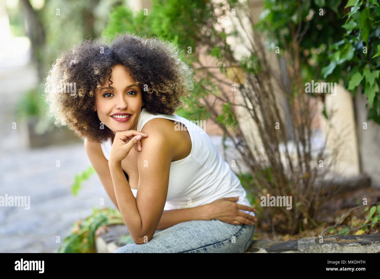 Mixed girl with afro hairstyle sitting in urban park. Young black woman ...