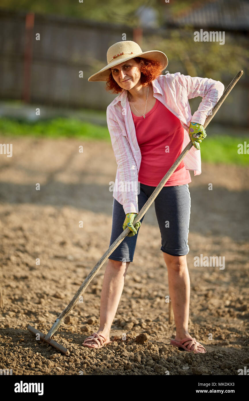 Caucasian lady farmer with a rake preparing the land for planting Stock ...