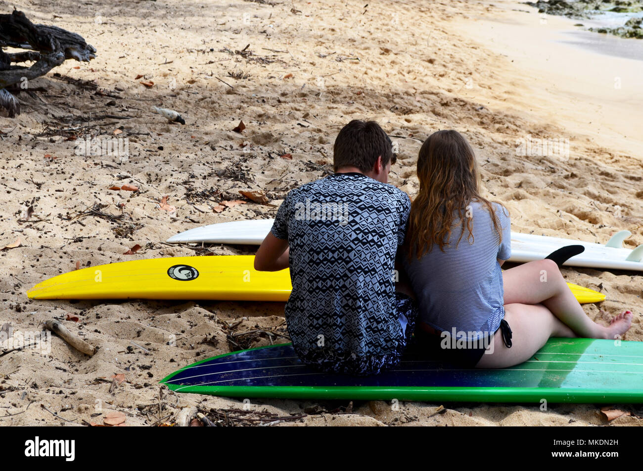 Young love. Two teenagers sitting together on a surf board at the beach ...