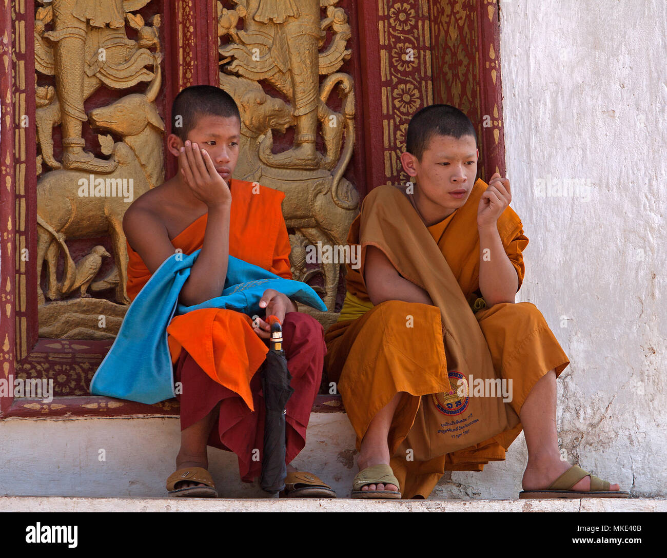 Two Buddhist monks sit on a step in front of a moanatery carved doorway ...