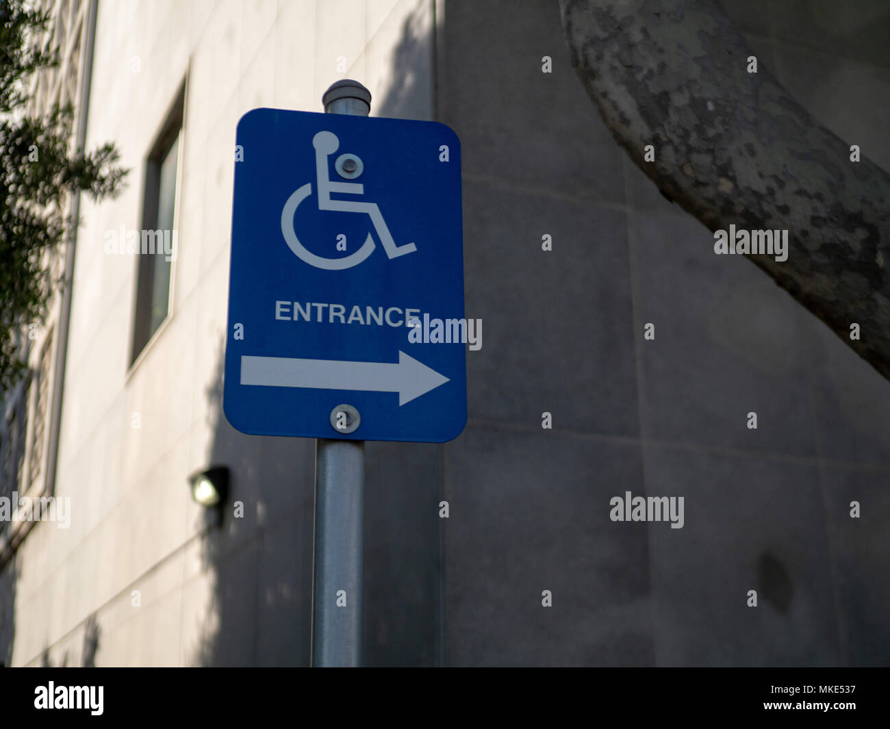Handicap entrance sign pointing to the right in a sunny outdoor area ...
