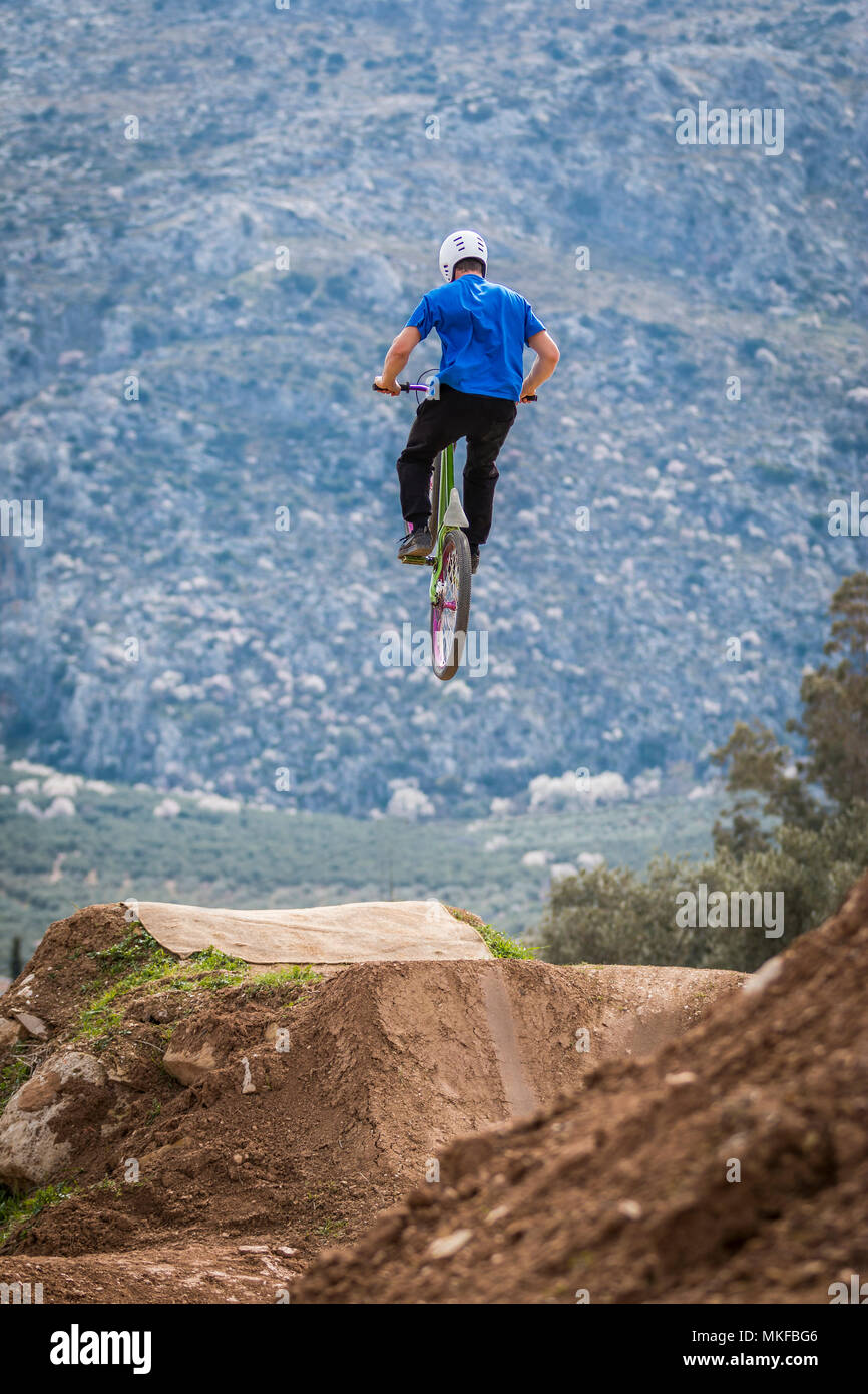 Rear view of sportsman on mountain bike flying over hill in the nature ...