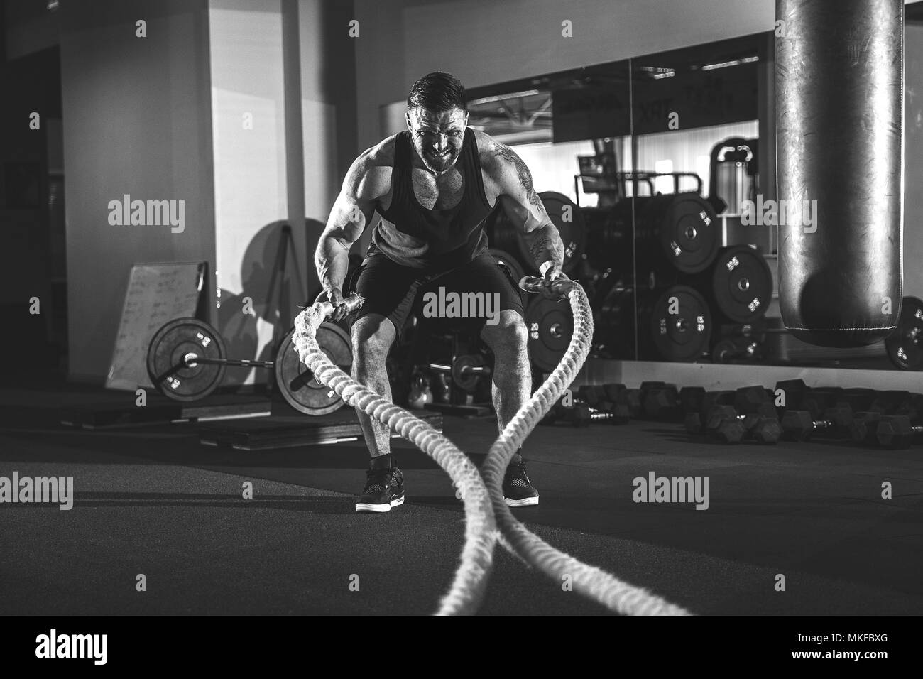 Muscular powerful aggressive man training with rope in functional ...