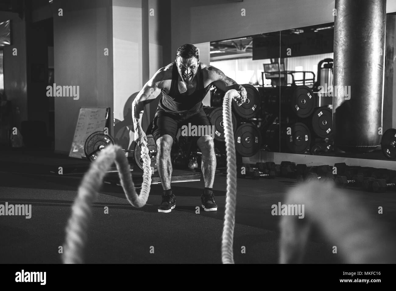 Muscular powerful aggressive man training with rope in functional ...