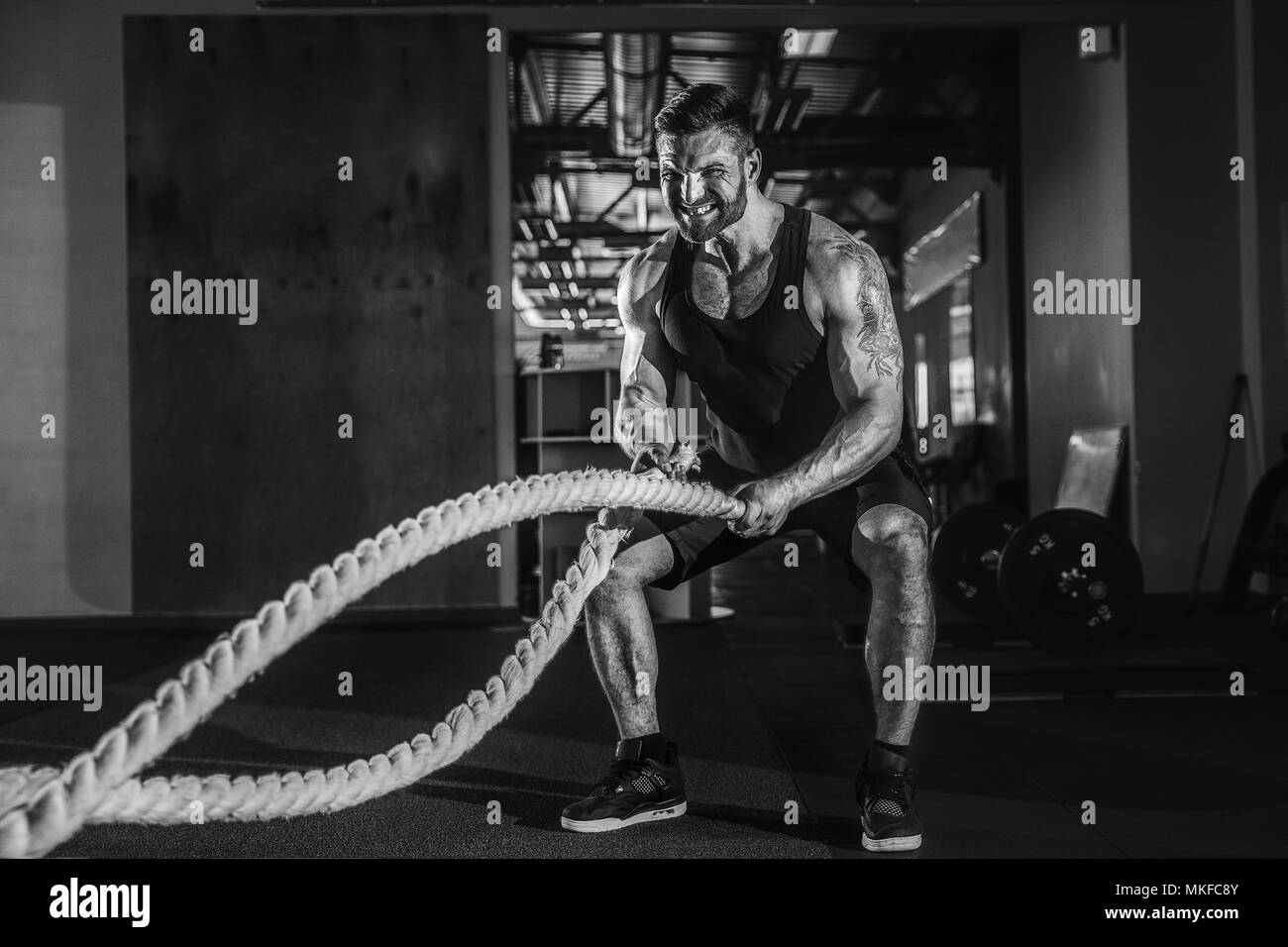 Muscular powerful aggressive man training with rope in functional ...