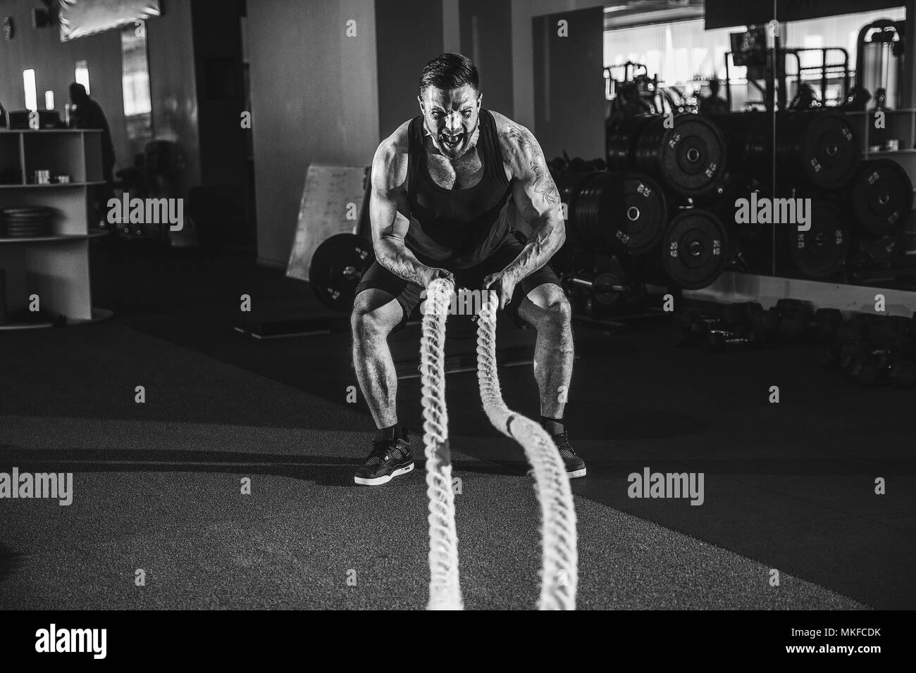 Muscular powerful aggressive man training with rope in functional ...