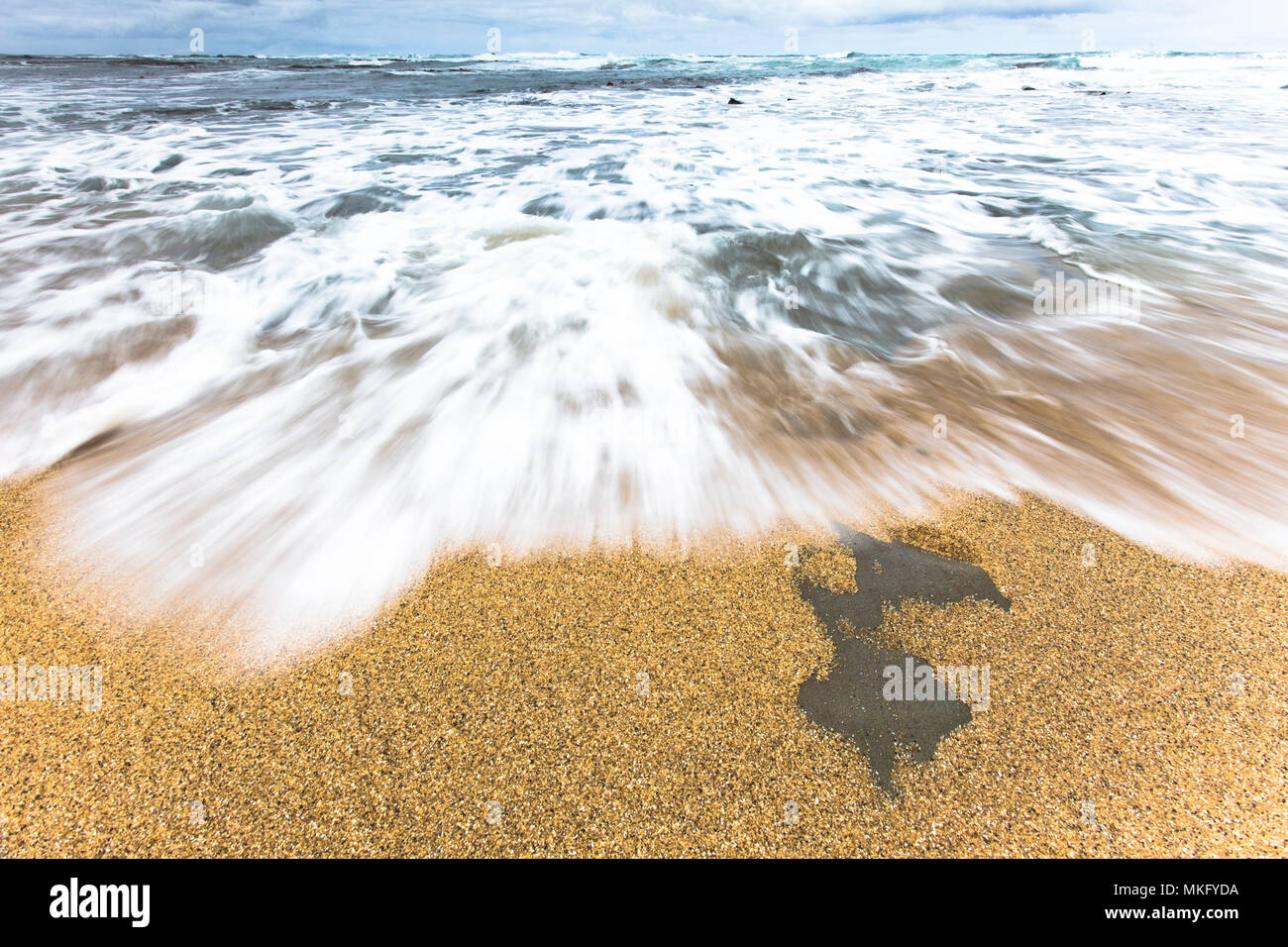 Ocean sea water rushing in to sandy beach shore on a cloudy blue sky ...