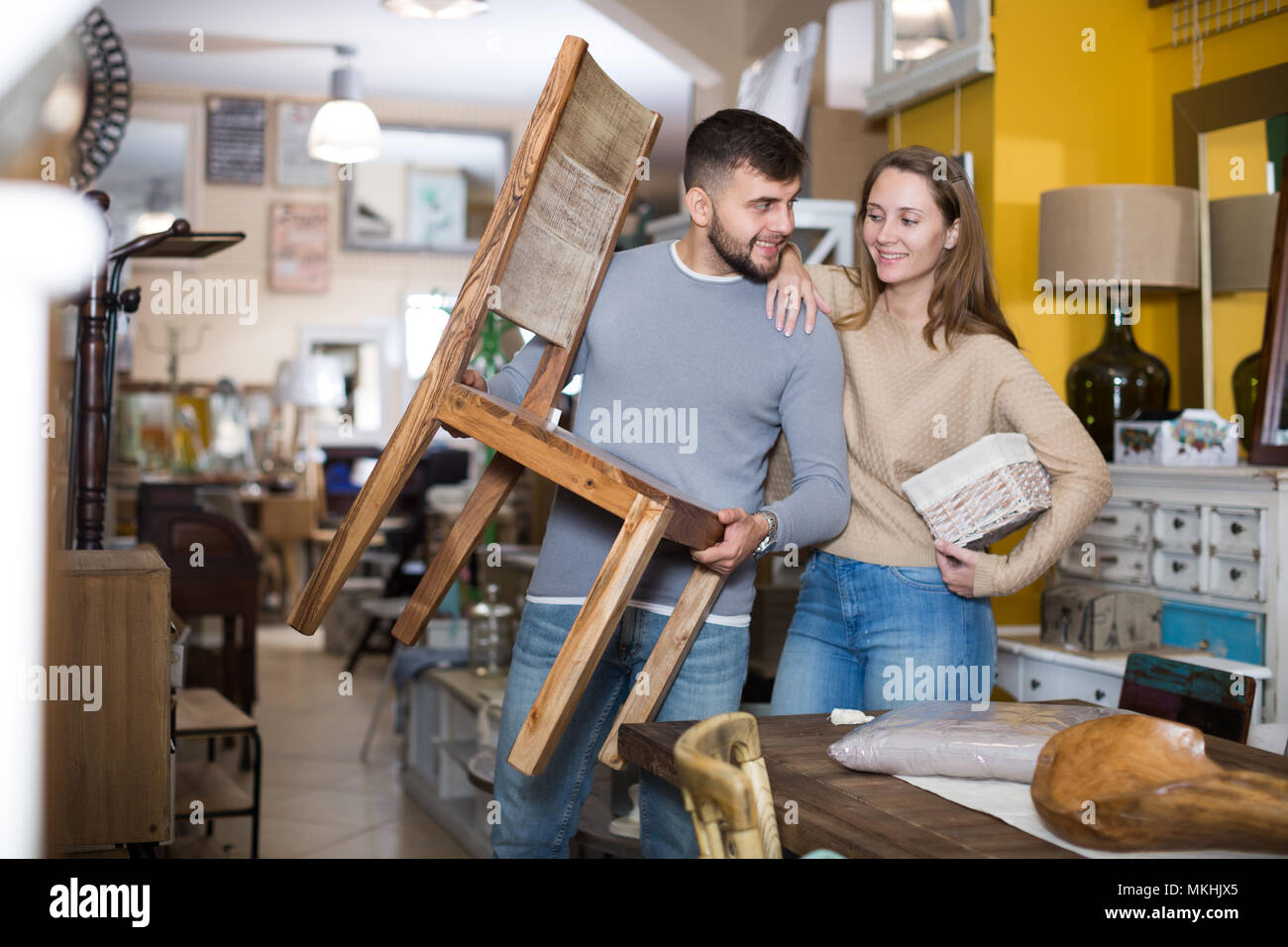 Young woman with boyfriend holding vintage chair in apartment crowded ...