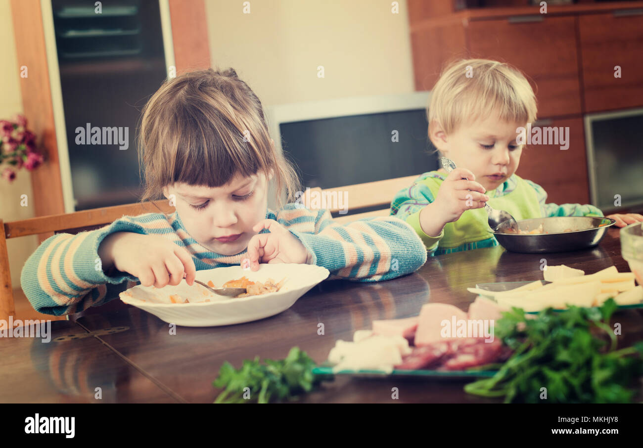 serious children eating food at wooden table in home interior Stock ...
