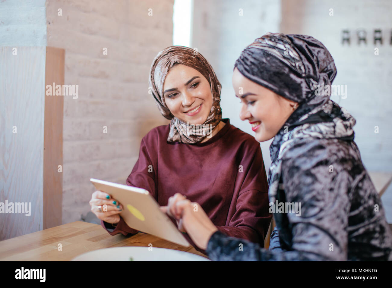 Two young Muslim women in cafe, shop online using electronic tablet ...
