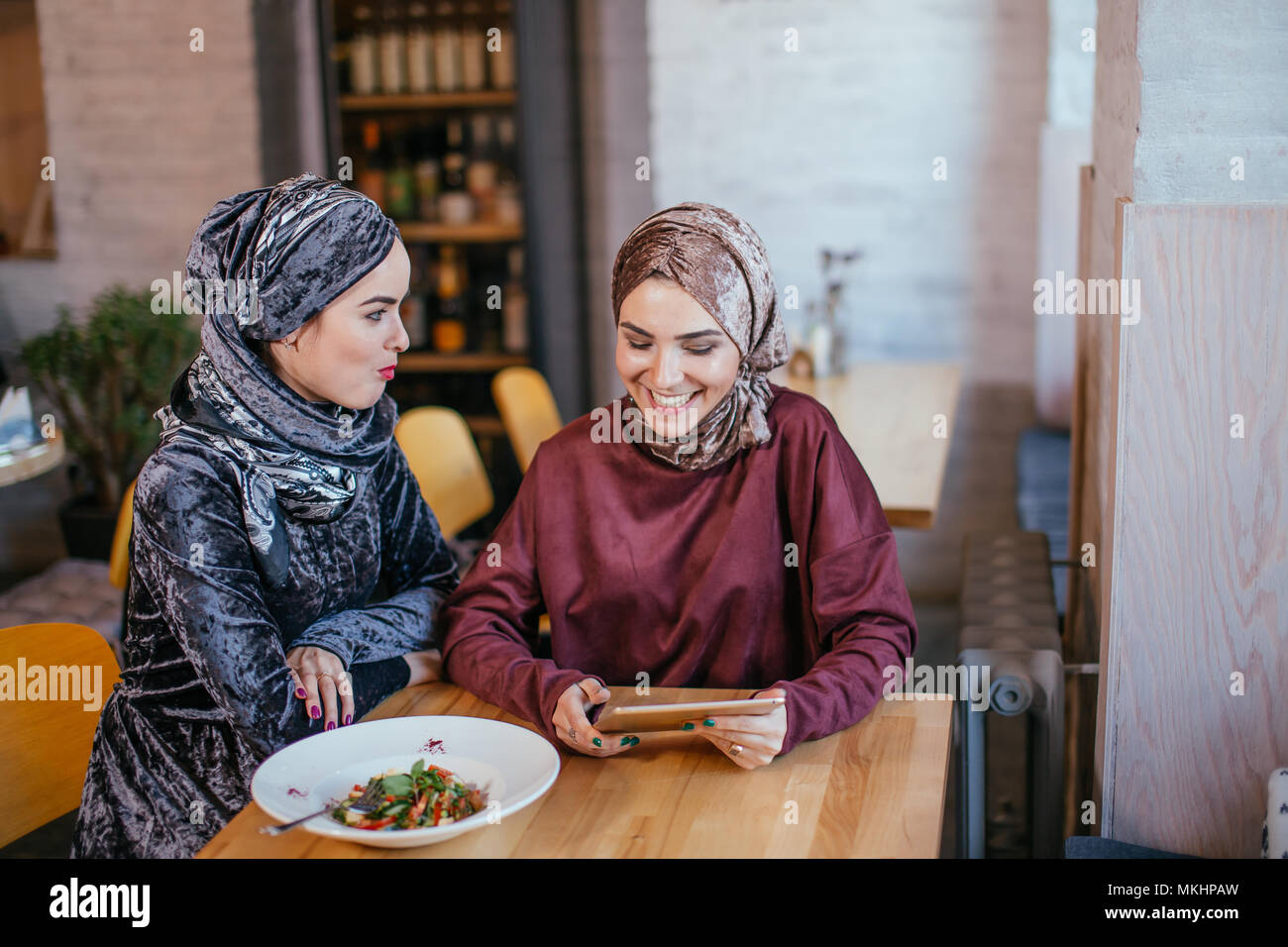 Two young Muslim women in cafe, shop online using electronic tablet ...