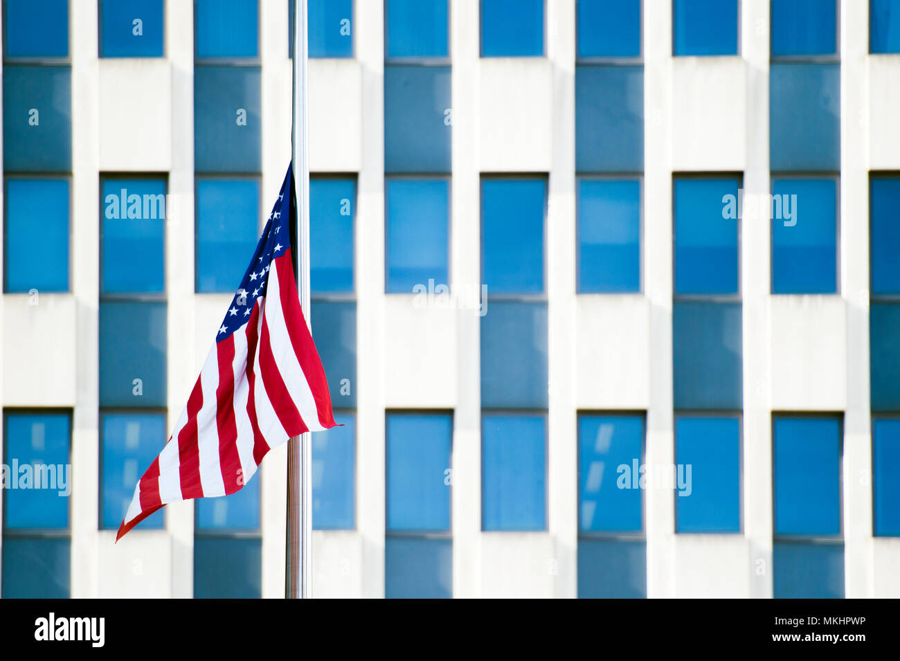 An American flag is waving on a blurred blue building full of windows ...