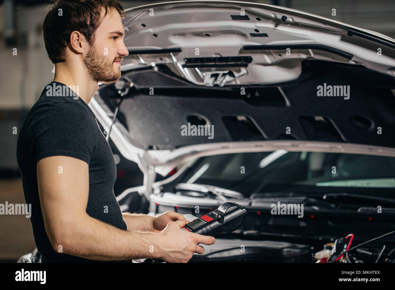 Car mechanic using electrical tool for testing car system in garage ...