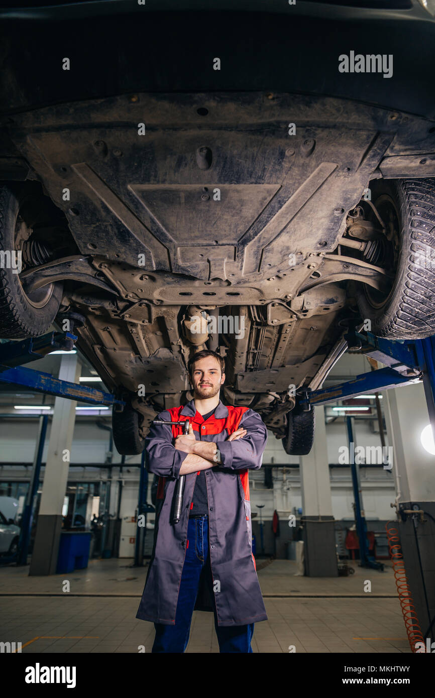 Auto mechanic crossed hands and looking at camera while standing under ...
