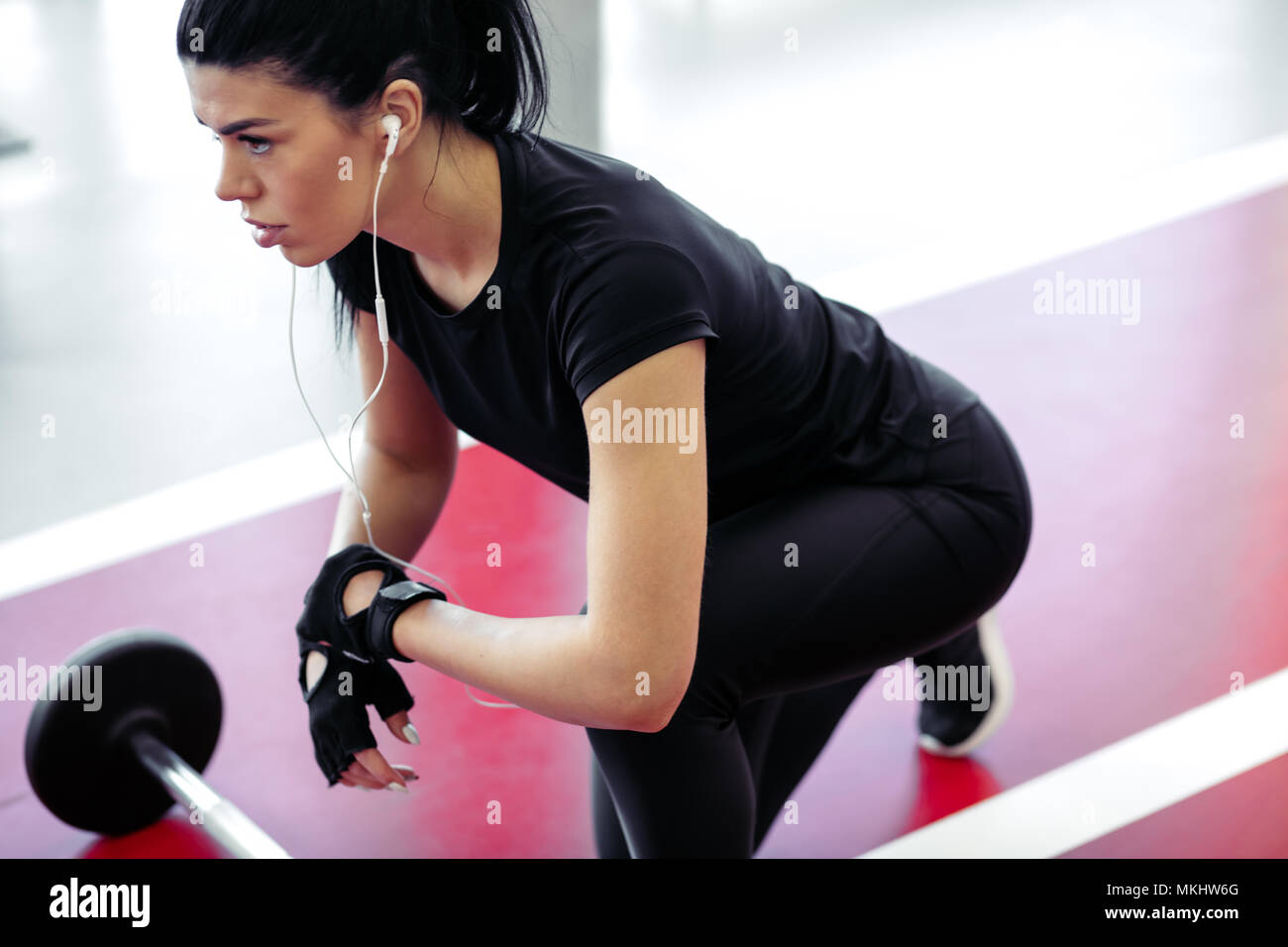 Young woman preparing for her weightlifting workout with small barbell ...