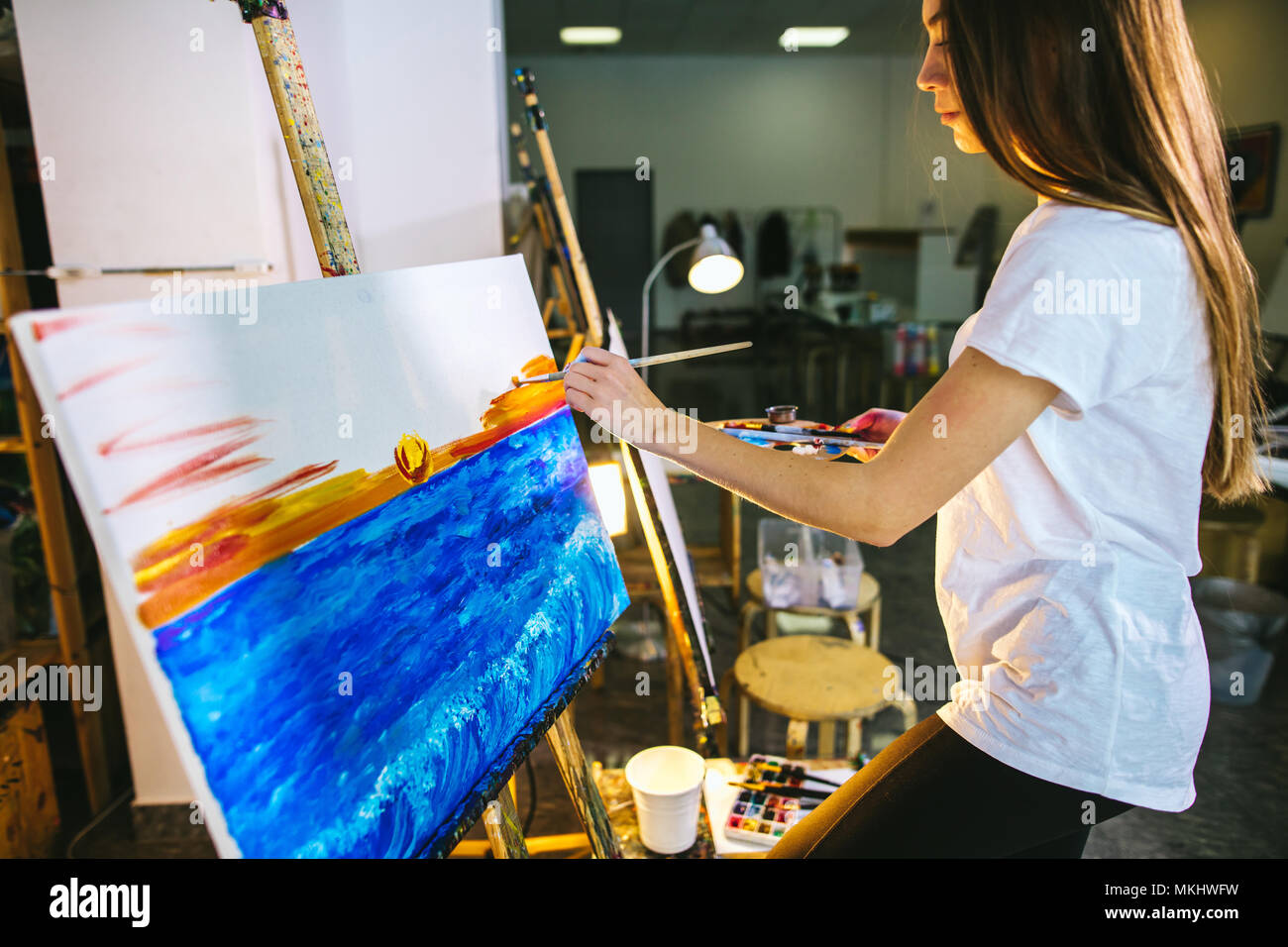 Long-haired artist woman with a palette in hands staying till night at ...