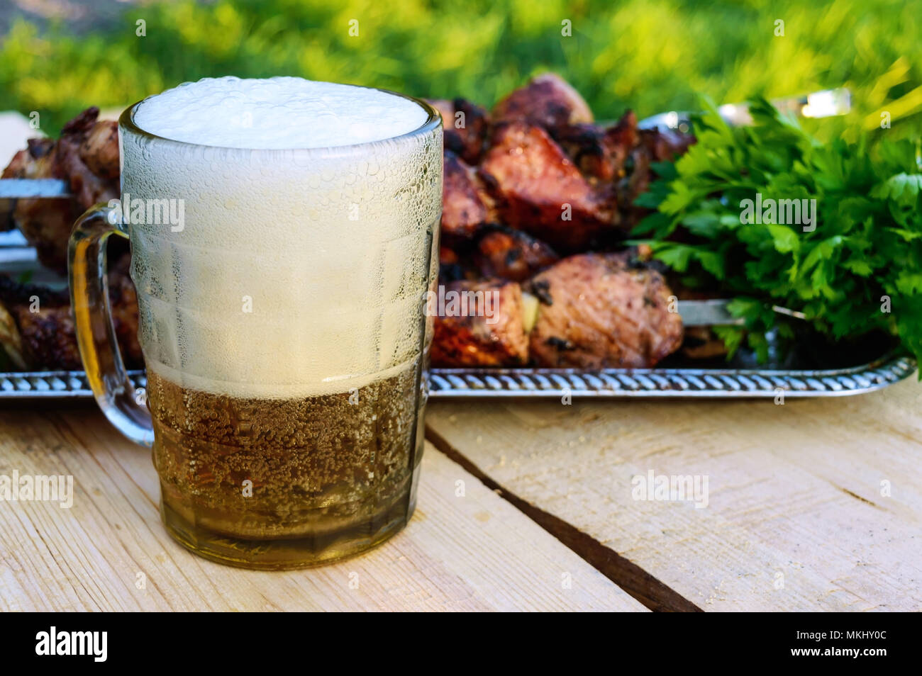 Foamy beer in a glass closeup grilled meat on skewers in the background ...