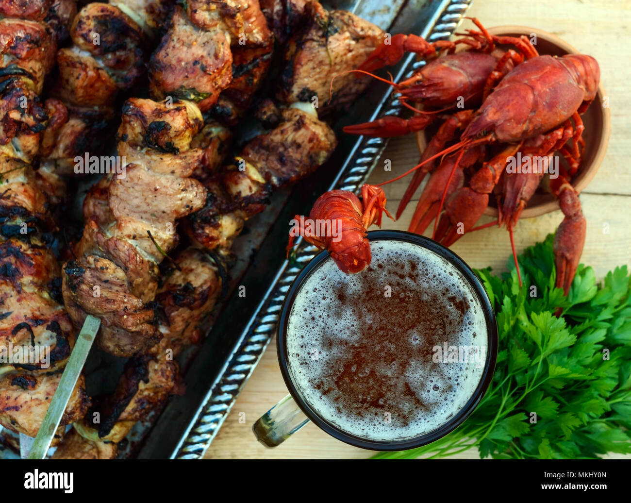 Foamy beer in a glass and boiled crawfish closeup, grilled meat on ...