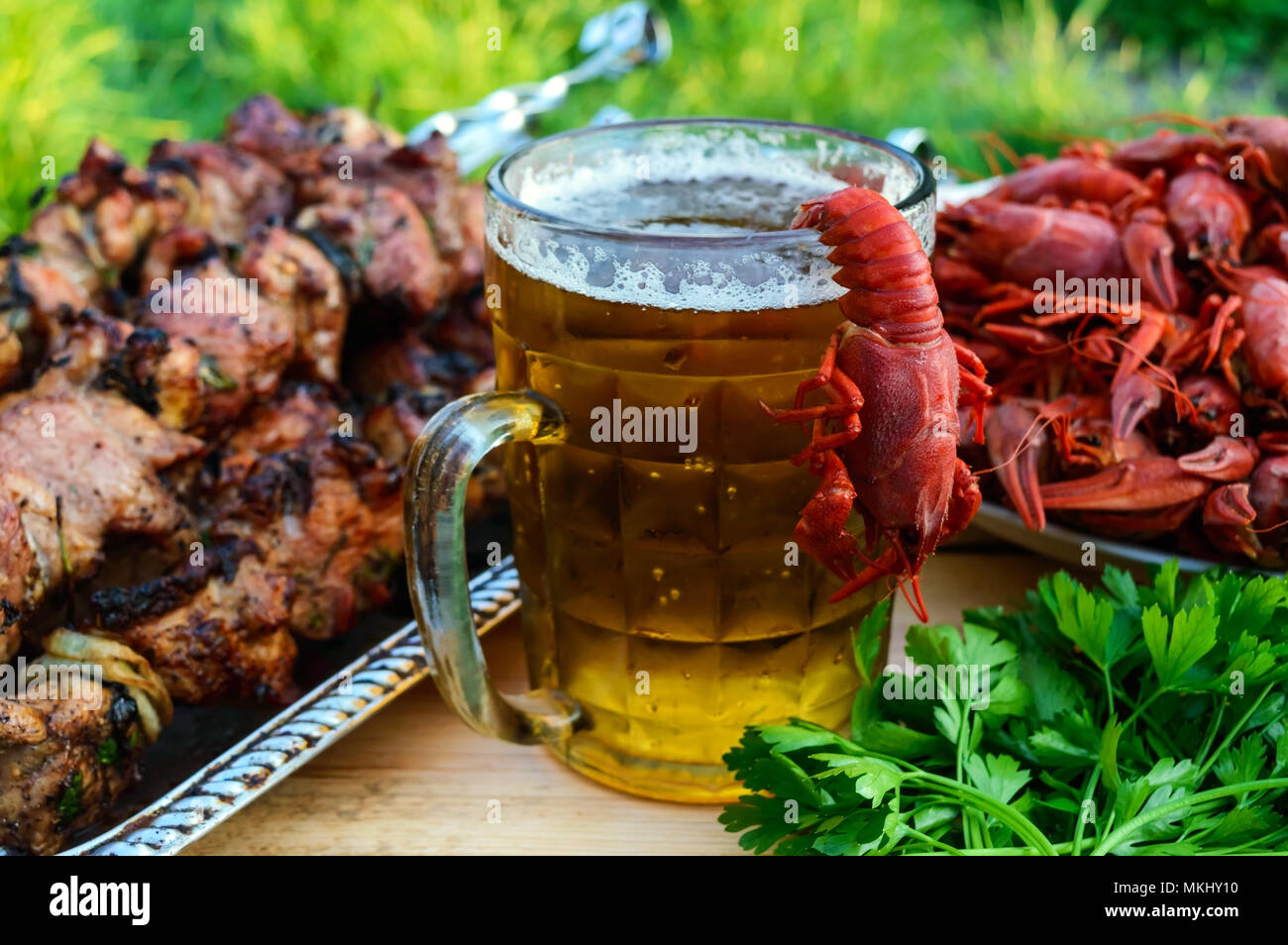 Foamy beer in a glass and boiled crawfish, grilled meat on skewers in ...